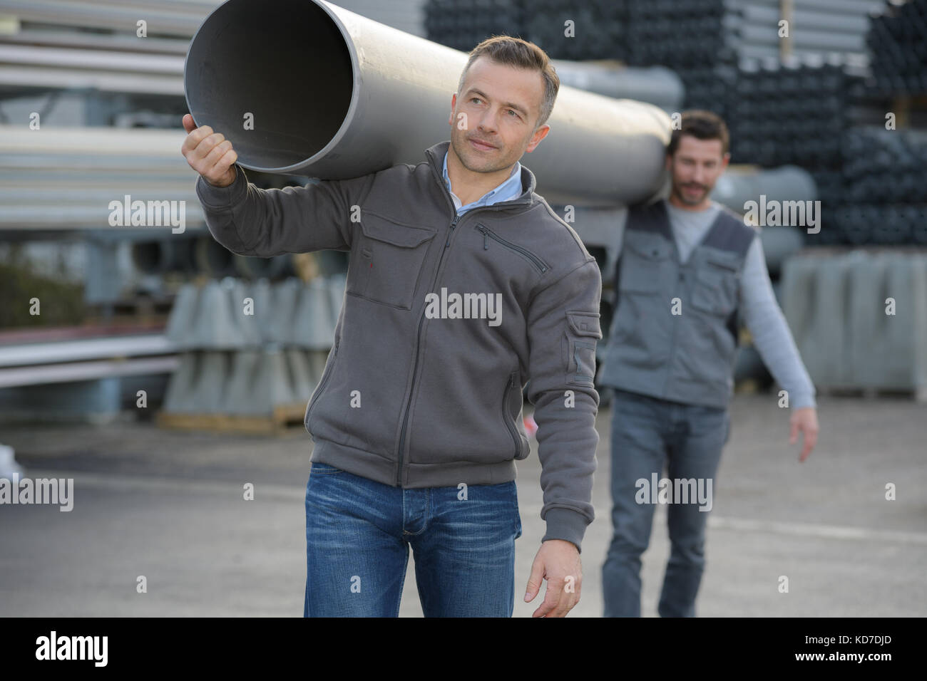 2 workers carrying pipe at factory warehouse Stock Photo - Alamy