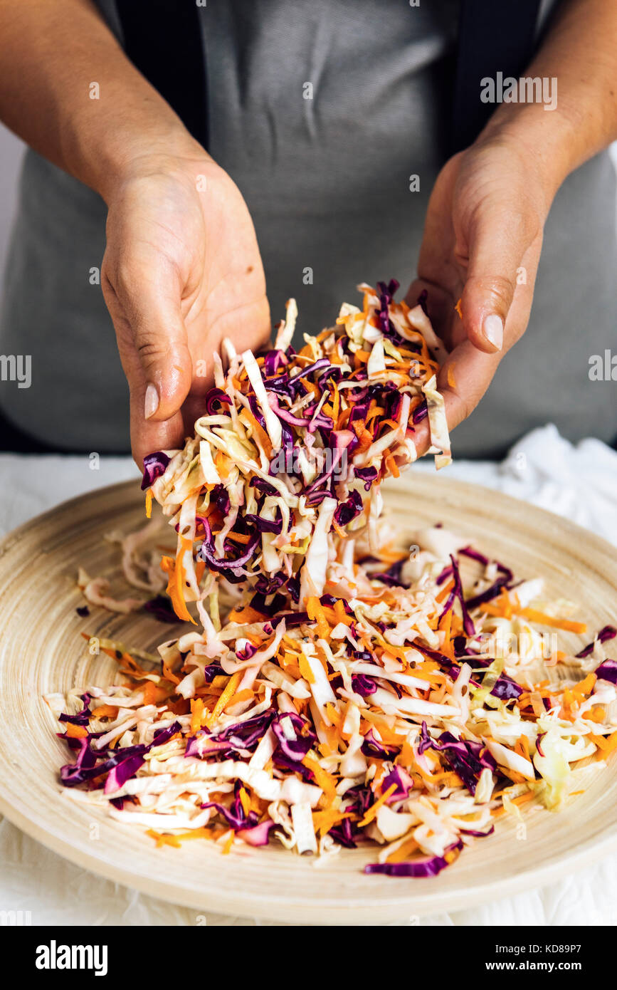 A woman tossing shredded carrot, white and purple cabbage in a wooden ...