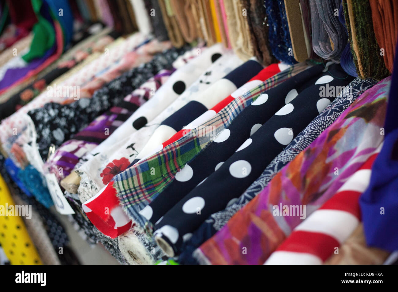 Various colorful rolls of clothing textile in a shop. The materials are ...