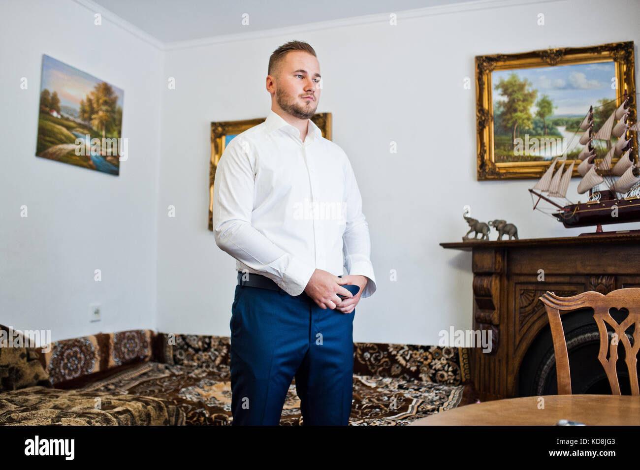 Portrait of a handsome groom dressing up in spacious luxurious room and ...