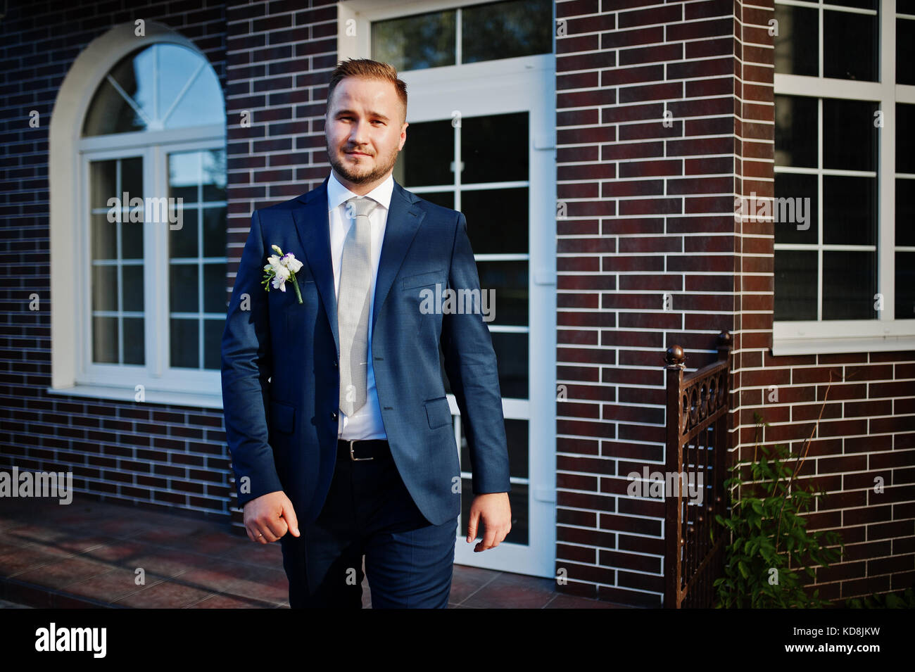 Portrait of a handsome young groom posing with a brick house on the ...