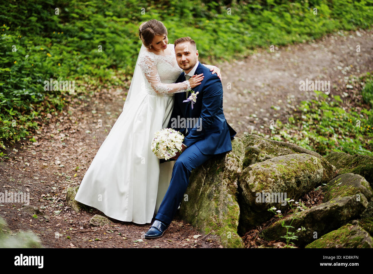 Magnificent bride sitting on a lap of her husband in the forest on a ...