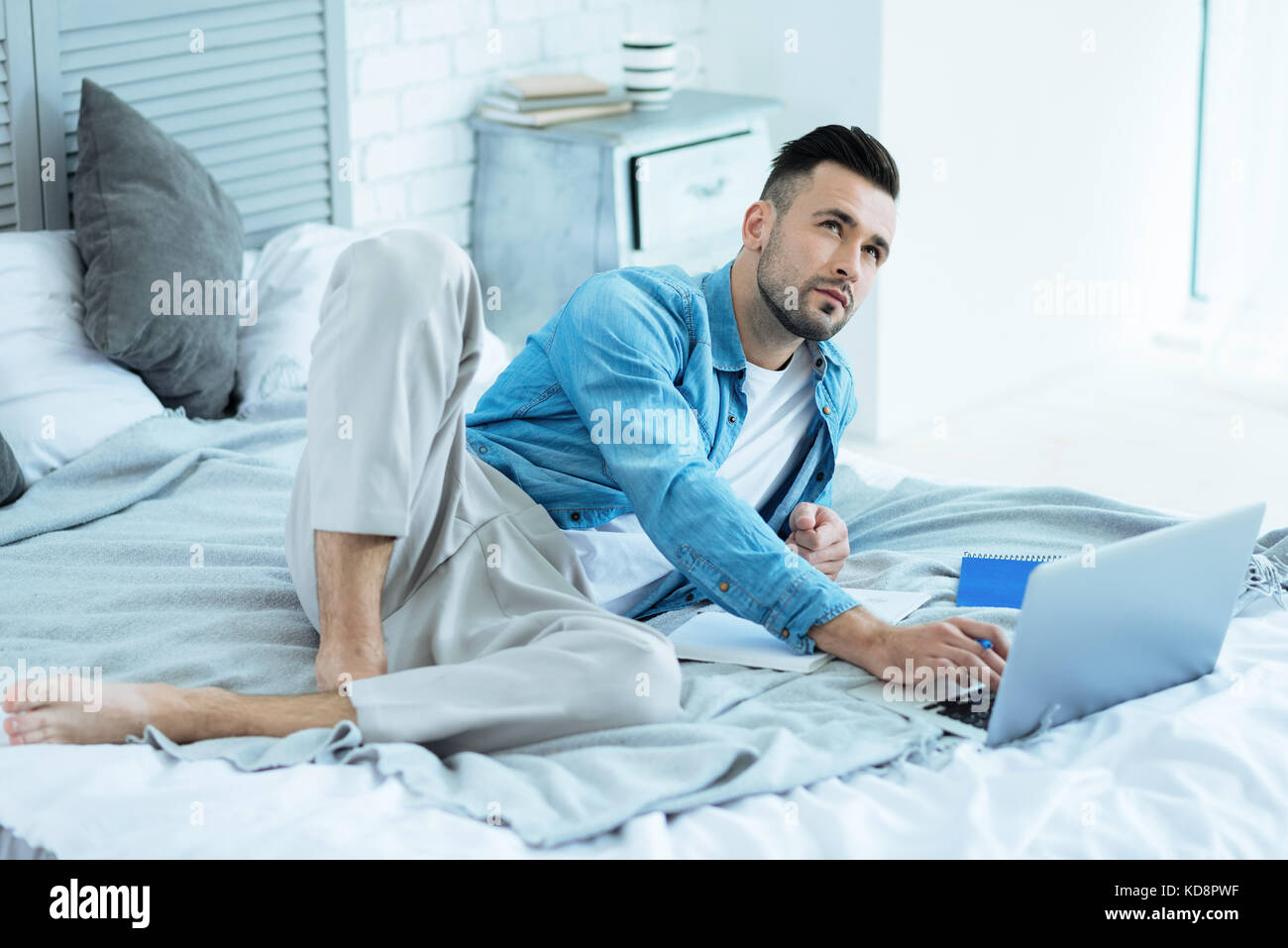 Pensive freelancer lying in bed while working from home Stock Photo - Alamy