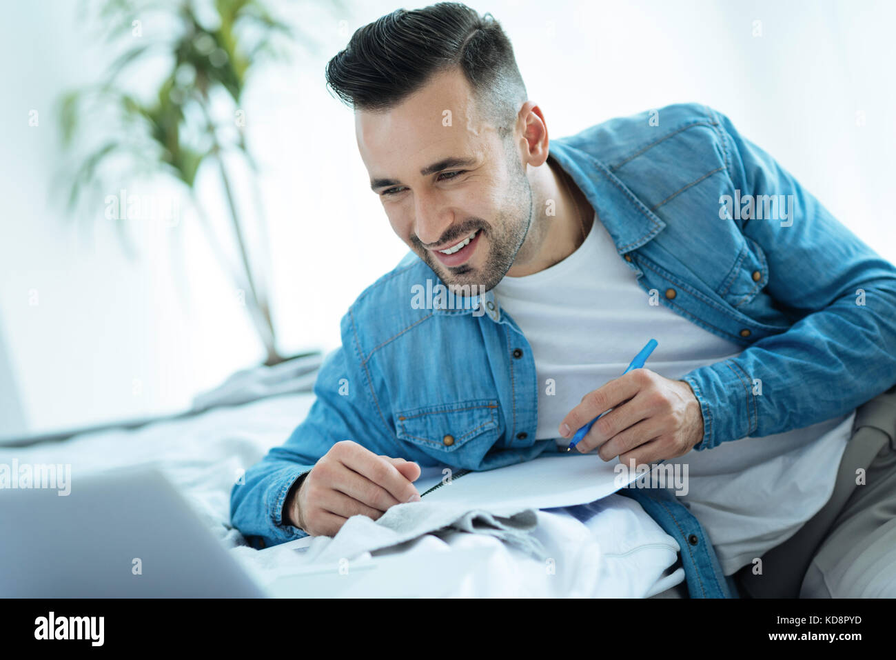 Smiling man looking at laptop while taking notes Stock Photo - Alamy