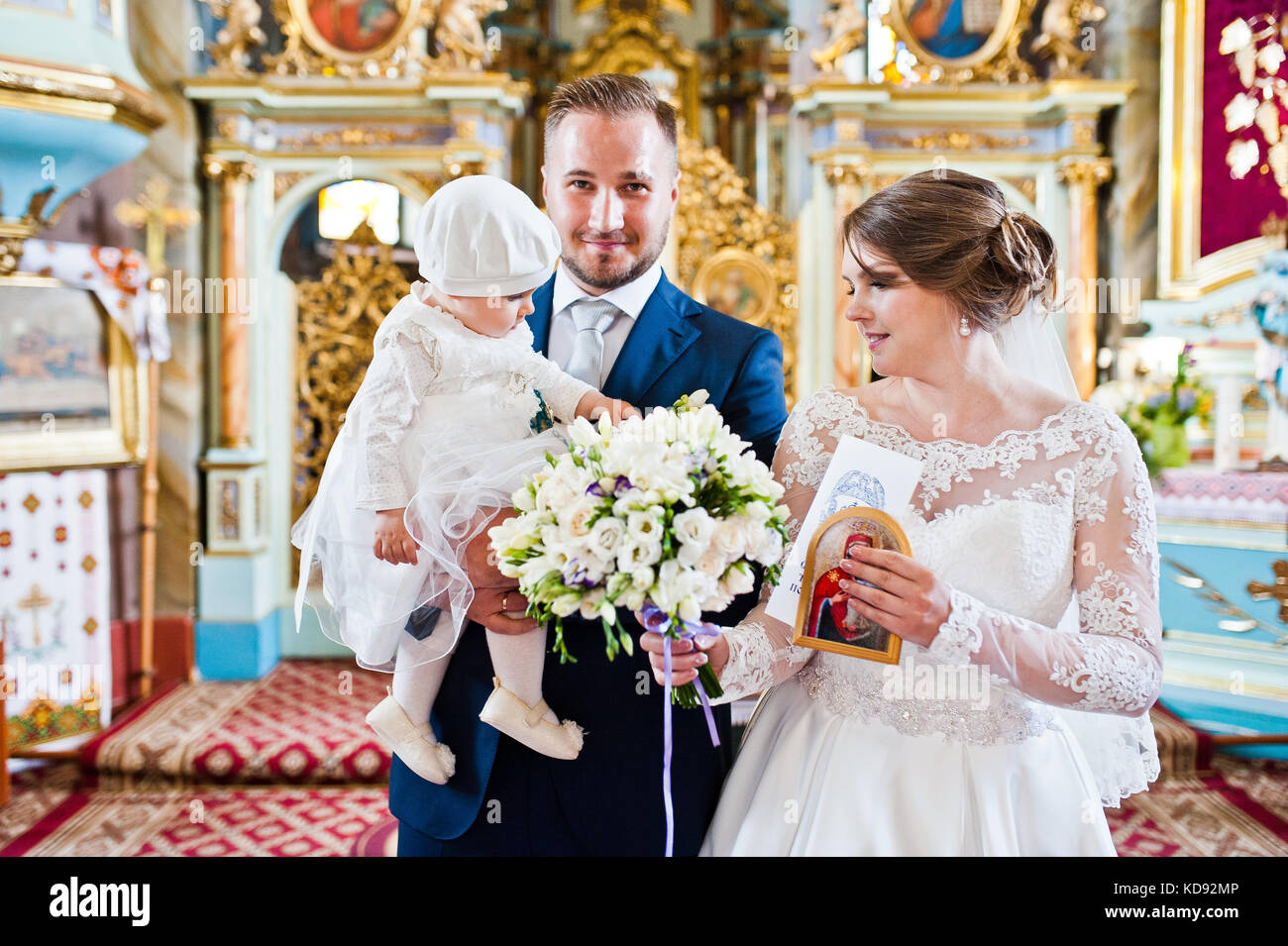Happy wedding couple in the church with their little baby daughter on ...