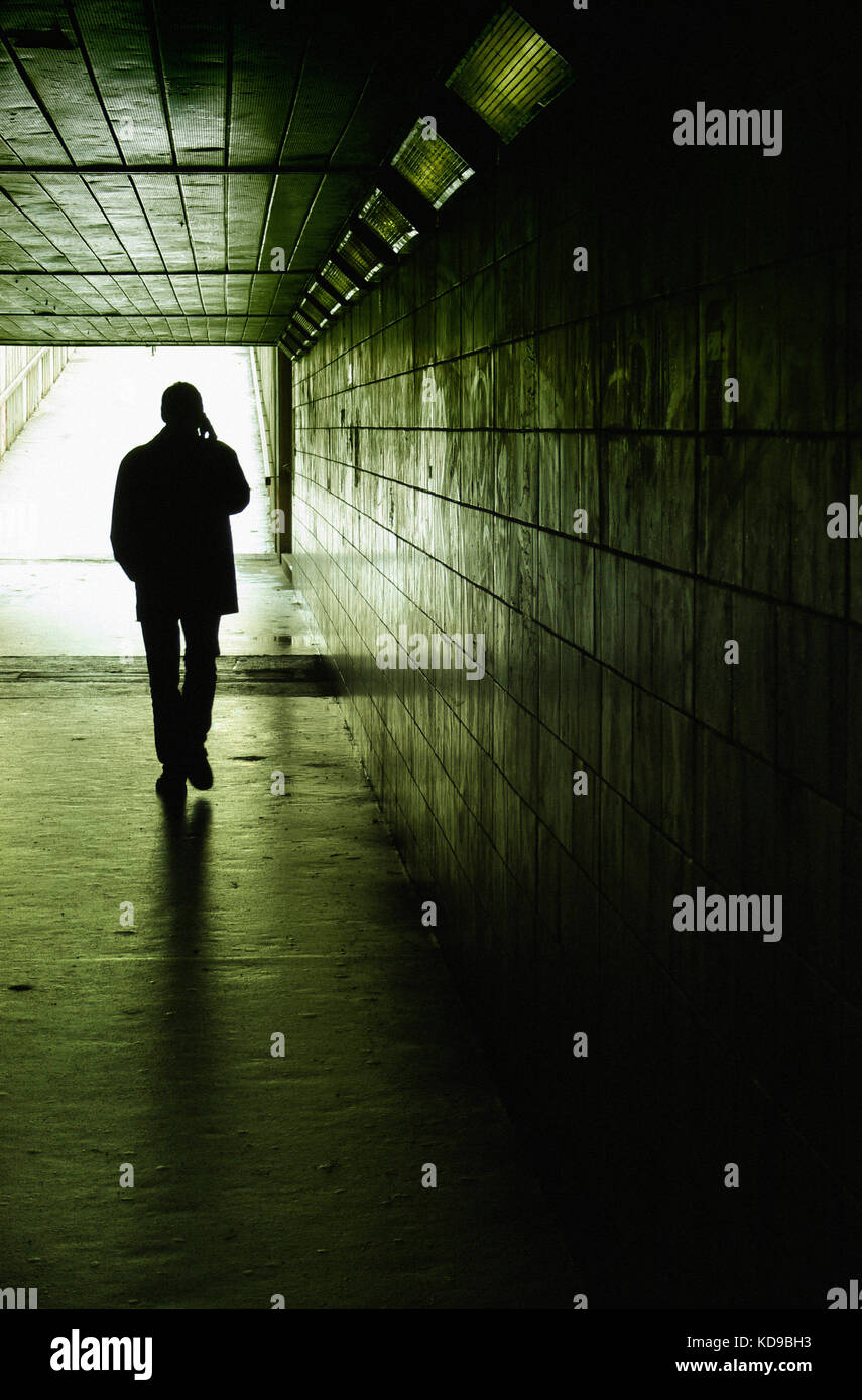 silhouette of a man talking on a cell phone under a walking passage ...