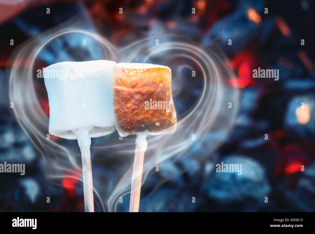 Two white sweet marshmallows roasting over fire flames. Smoke in form ...