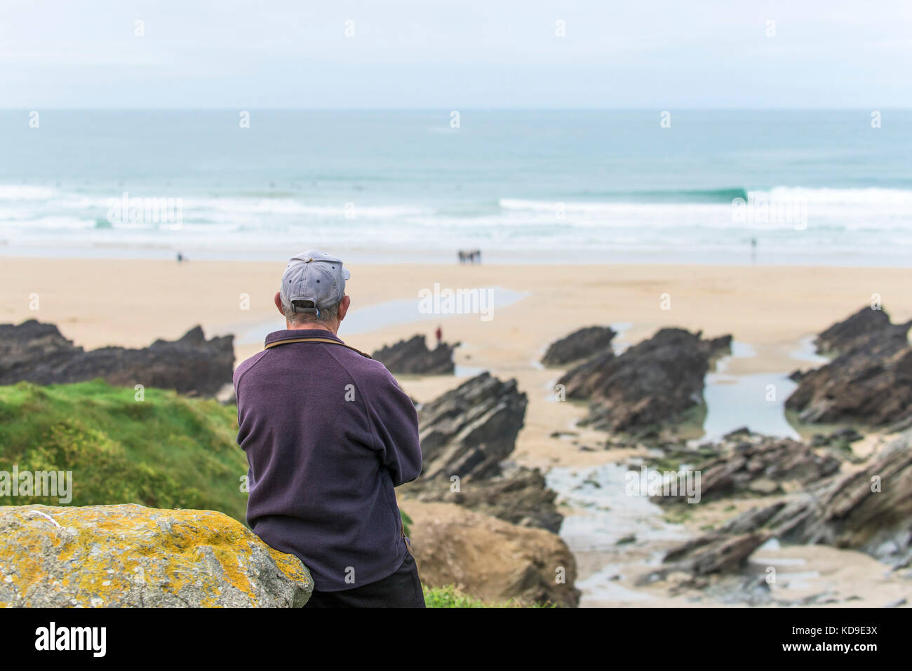 A man looking out to sea - a man leaning against a granite rock and ...