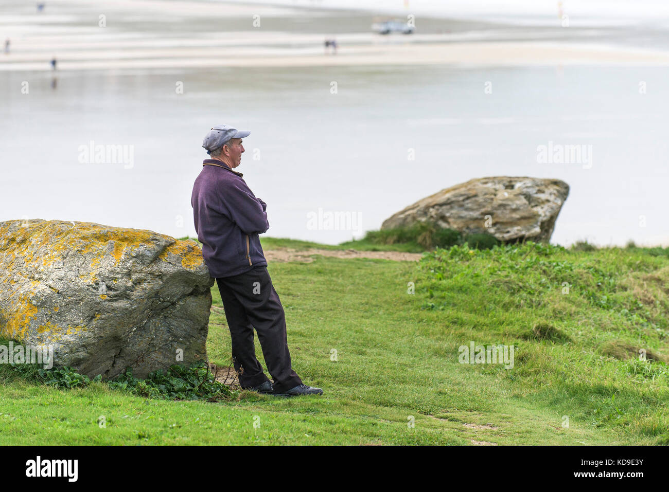 A man looking out to sea - a man leaning against a granite rock and ...