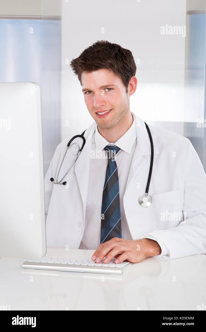 Portrait Of Happy Male Doctor Using Computer At Desk In Clinic Stock ...