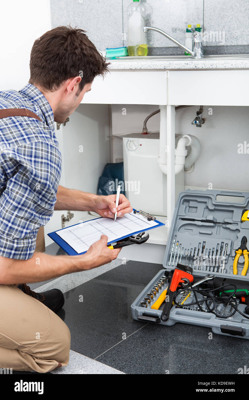 Handsome Young Plumber Writing On Clipboard With Pen In Kitchen Room ...
