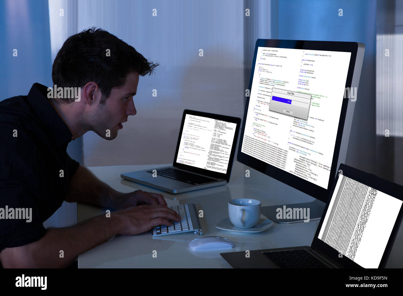 Young Man Sitting At Desk Working On Computer And Laptop At Home Stock ...
