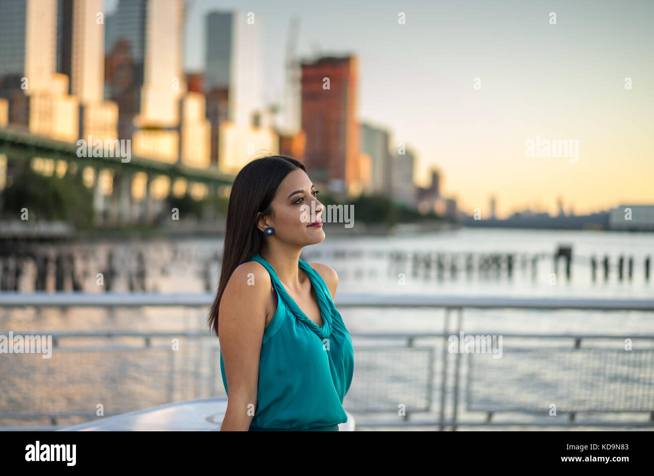 Beautiful girl enjoying sunset in the riverside park with city highrise ...