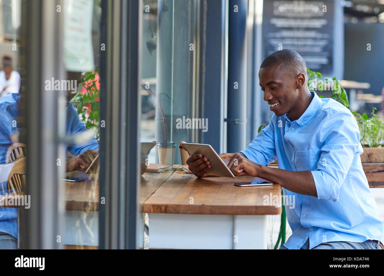 Young African man working online at a sidewalk cafe table Stock Photo ...