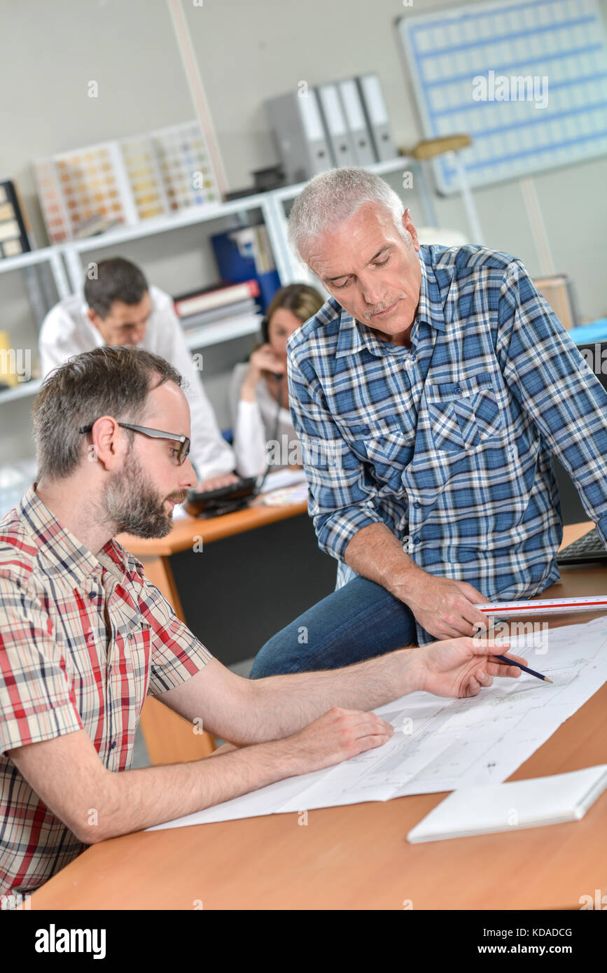 Two men discussing paperwork, one sitting on desk Stock Photo - Alamy