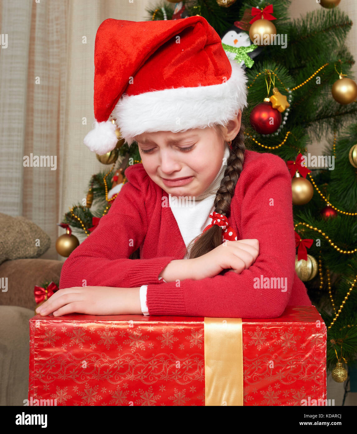 Unhappy girl shed tears near christmas tree, dressed in red and santa ...