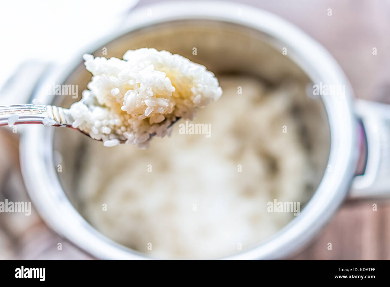Macro closeup of spoonful of fresh cooked rice by cooking pot on table ...