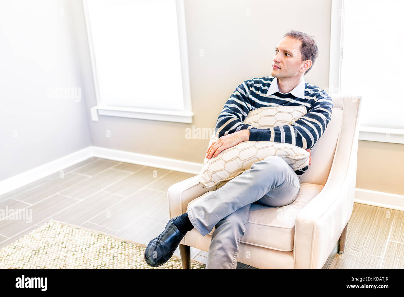 Young thoughtful thinking man sitting on couch hugging pillow in modern ...