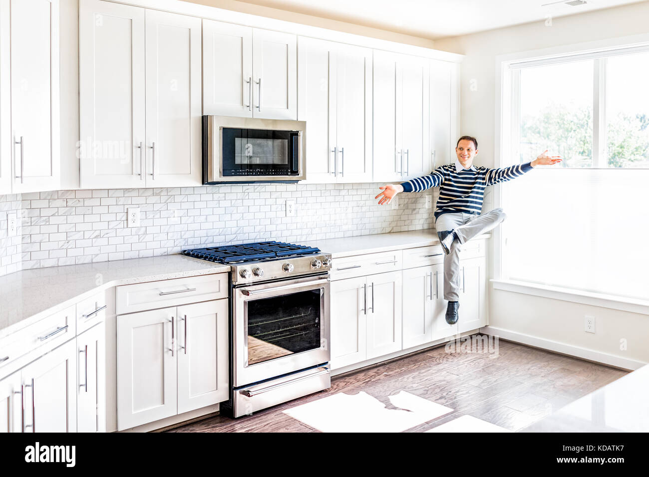 Young man sitting on kitchen countertop with outstretched open arms in ...