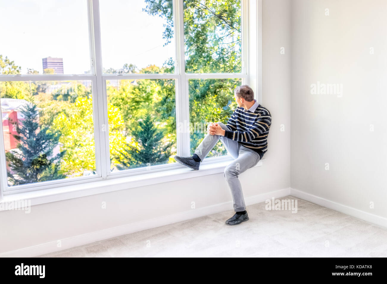 Young man sitting on windowsill by large window overlooking red brick ...