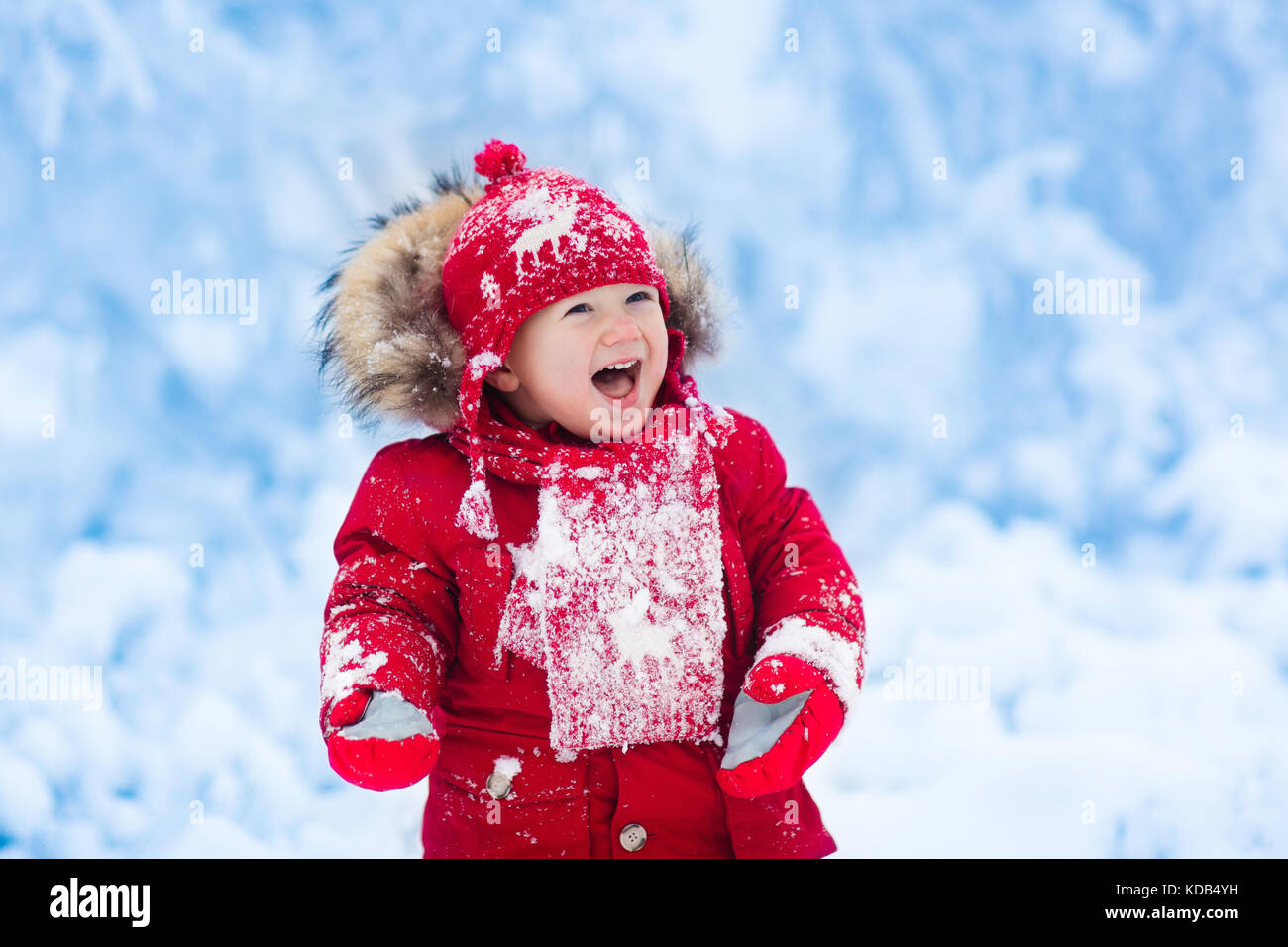 Baby playing with snow in winter. Little toddler boy in red jacket and ...