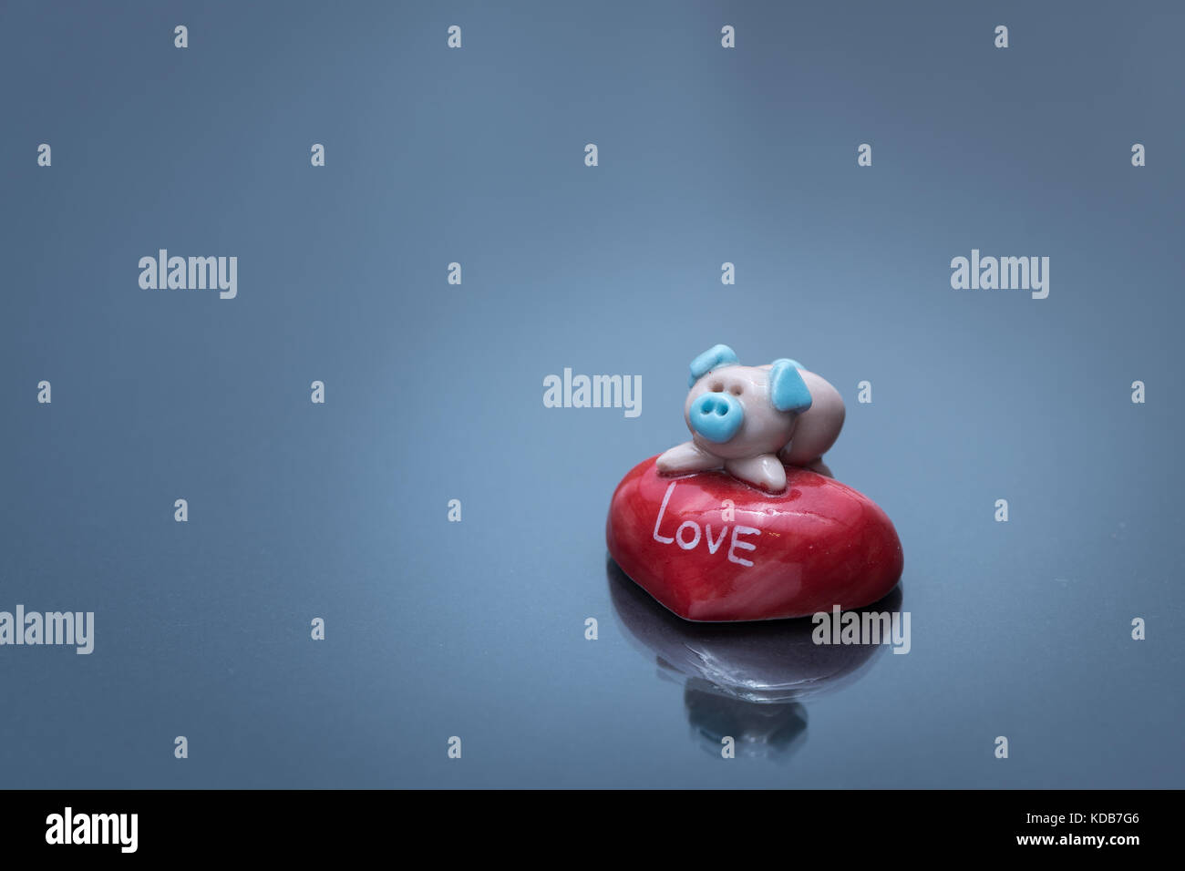 Figurine of a cute little pig lying on a red heart-shaped stone with ...
