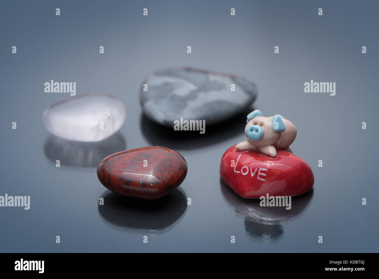 Figurine of a cute little pig lying on a red heart-shaped stone with ...