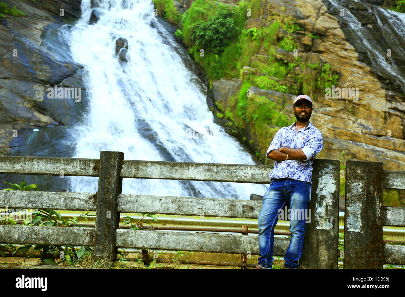 Young man smiling and standing in pose with big waterfall in the ...