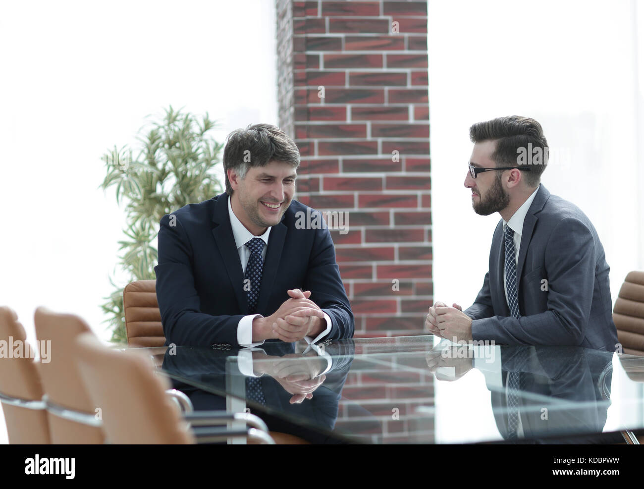 Two businessmen discussing tasks sitting at office table Stock Photo ...