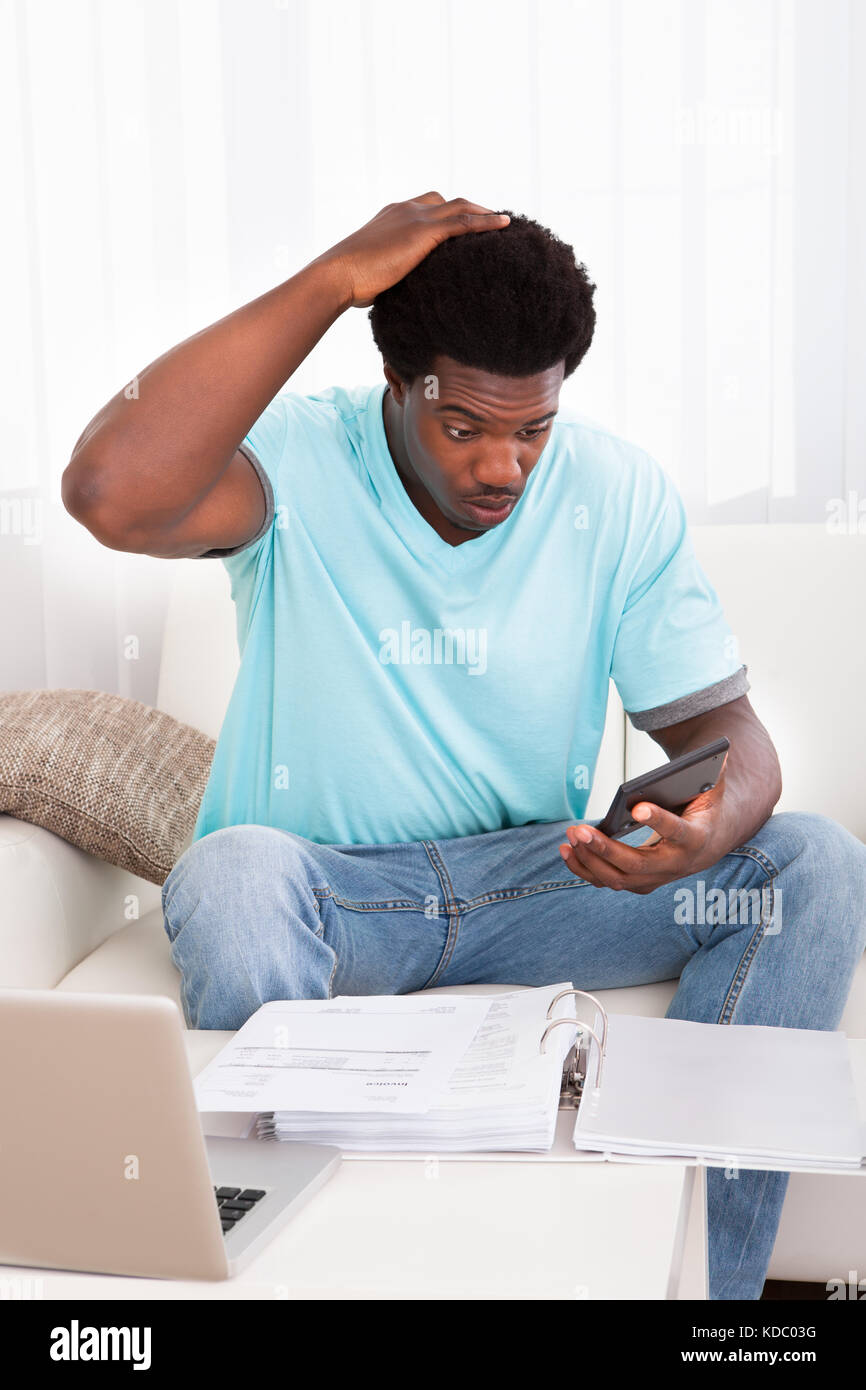 Portrait Of A Worried Young African Man Holding Calculator Working At ...