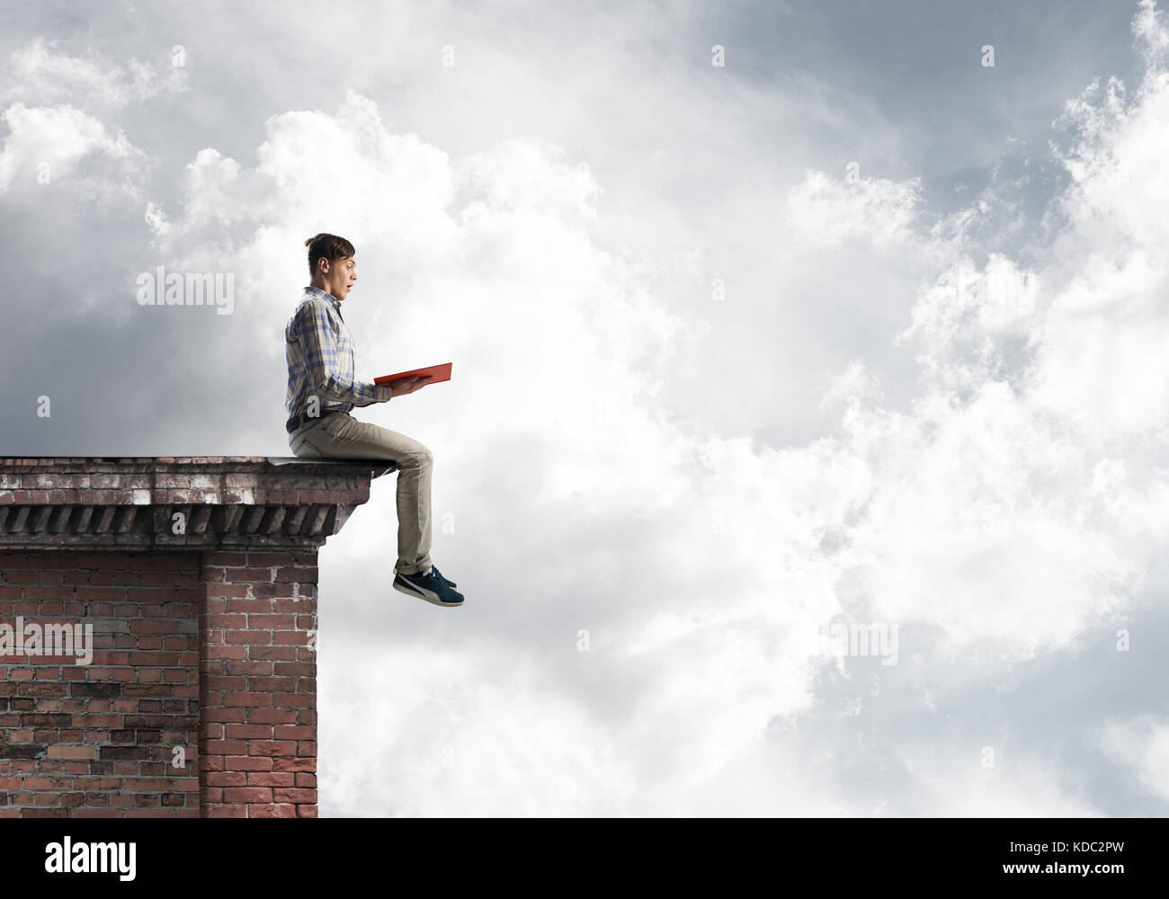 Man on roof edge reading book and cloudscape at background Stock Photo ...