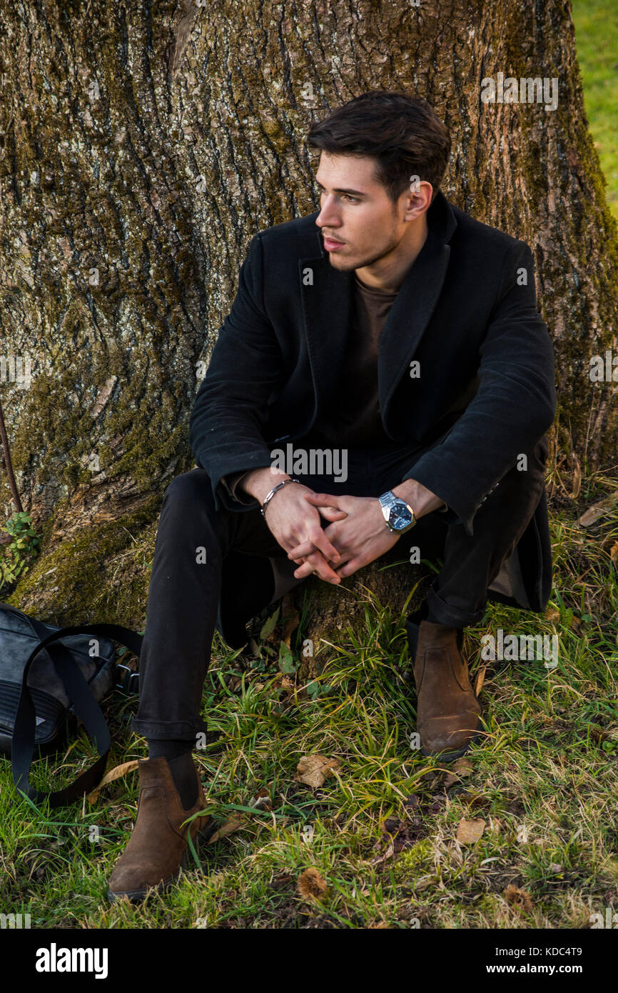 Handsome young man leaning against tree Stock Photo - Alamy