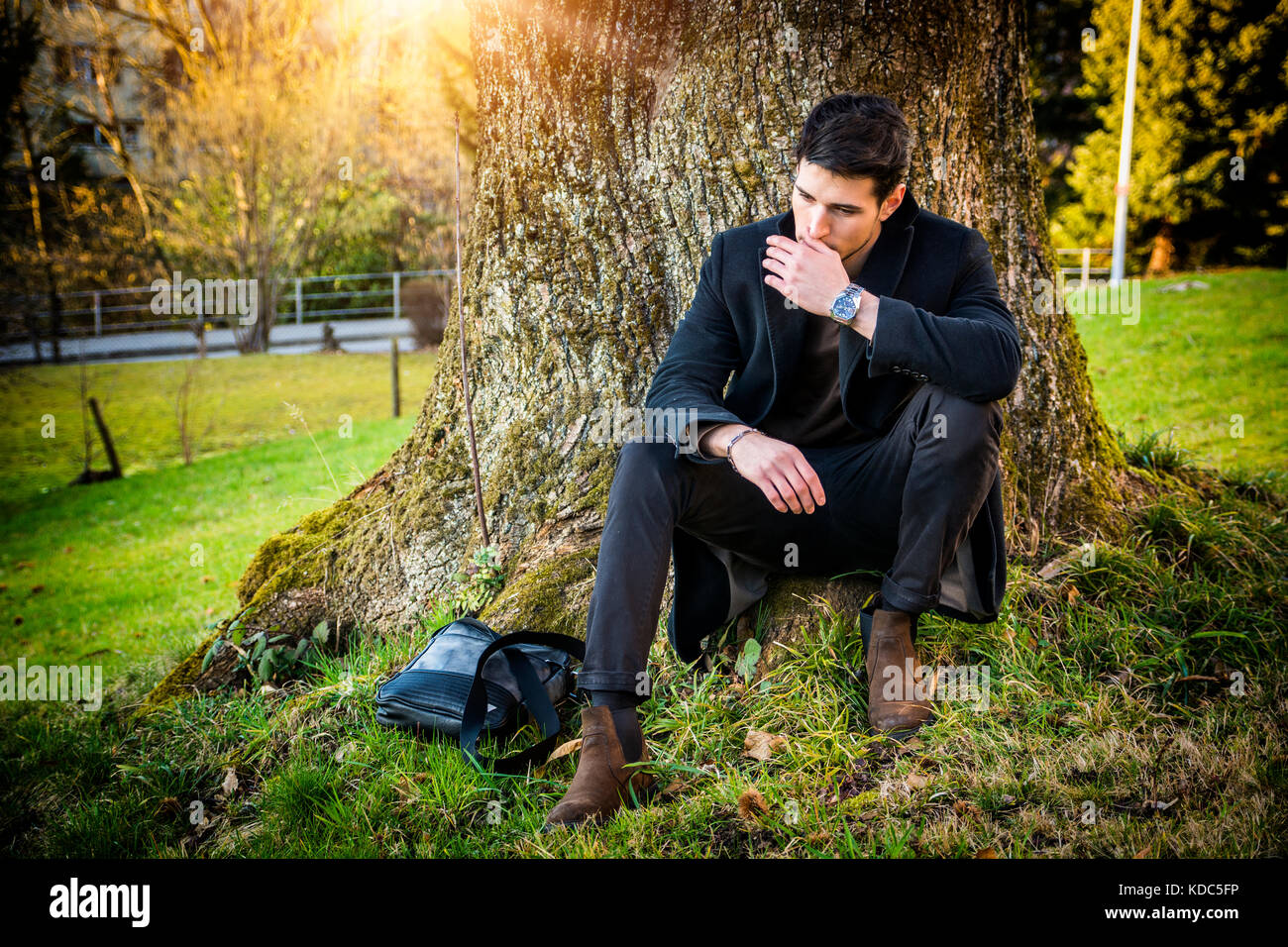 Handsome young man leaning against tree Stock Photo - Alamy