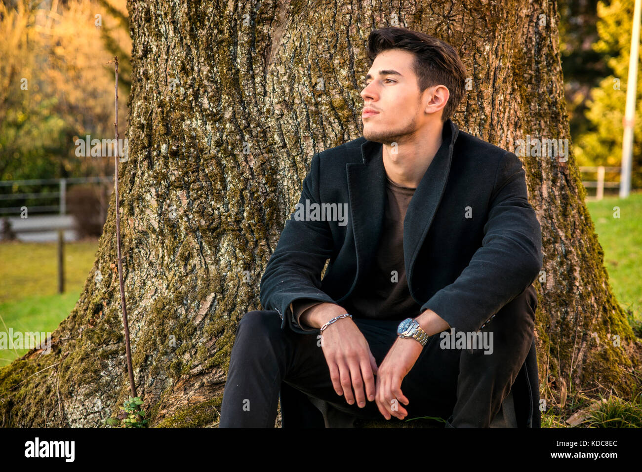 Handsome young man leaning against tree Stock Photo - Alamy