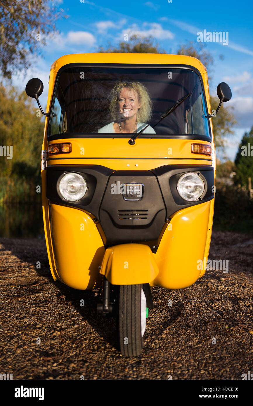 A blonde woman drives a yellow tuk tuk in an English village Stock ...