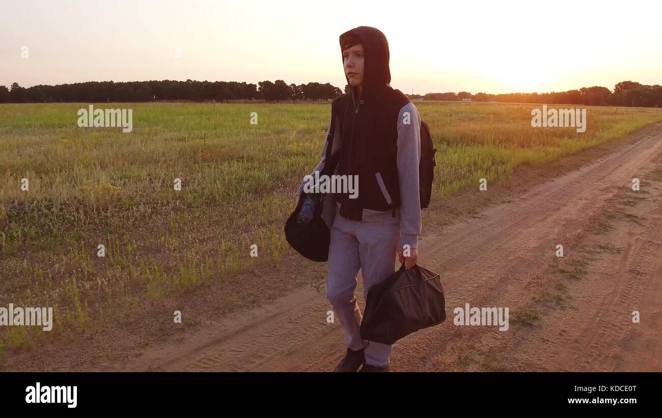 Boy teen traveling. Boy teenage tramp walking along the road in a hood ...