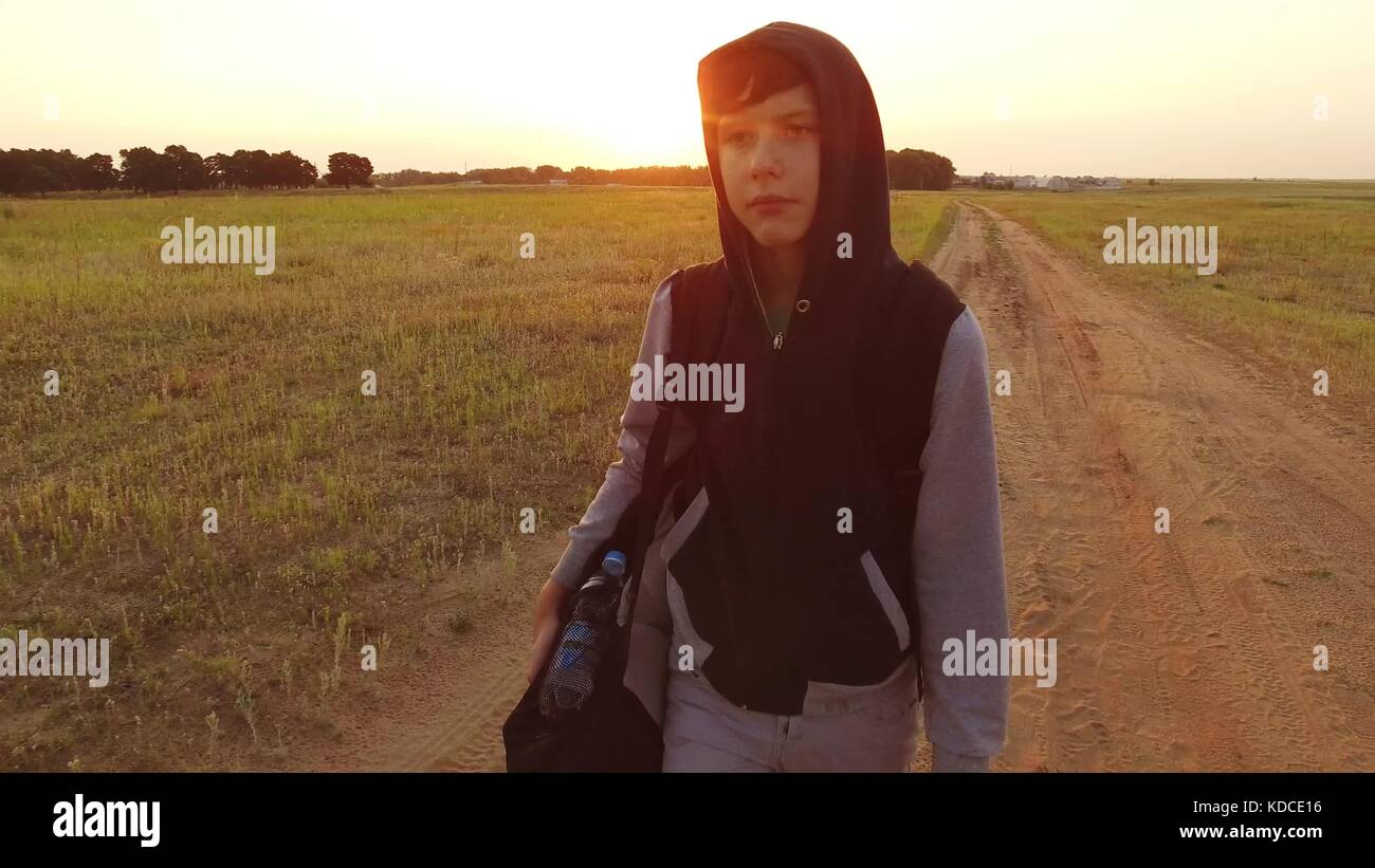 Boy teen traveling. Boy teenage tramp walking along the road in a hood ...