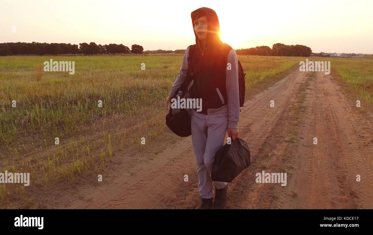 Boy teen traveling. Boy teenage tramp walking along the road in a hood ...