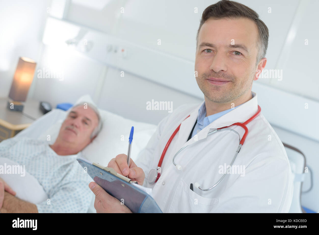 Doctor making notes, patient in background Stock Photo - Alamy