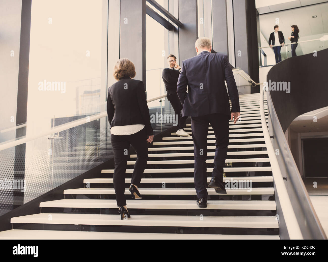 Modern business people walking on stairs in glass hall of office ...