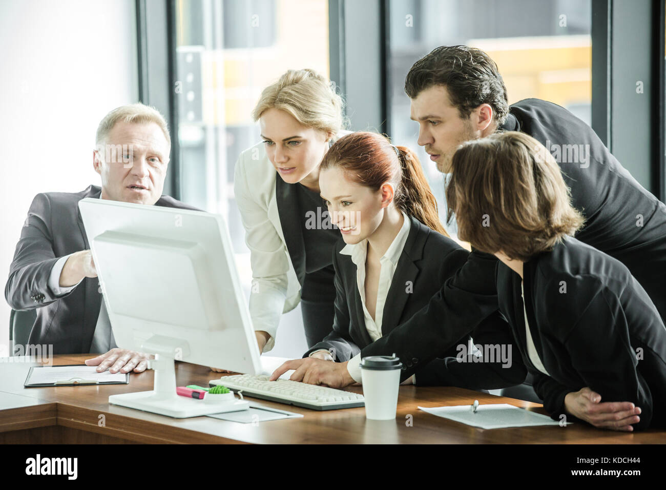 Business team look at one computer monitor having discussion in office ...