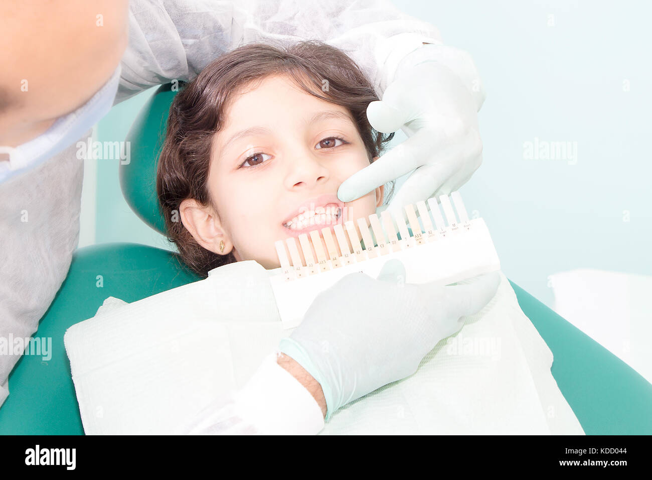 Dentist choosing a color of a teeth for young girl at dental clinic ...