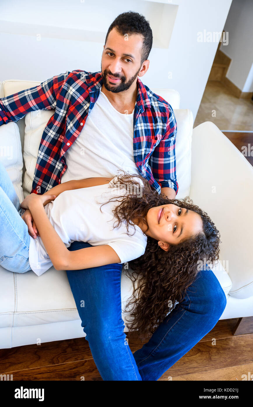 A young afro teenage girl leaning in her fathers lap on a couch Stock ...