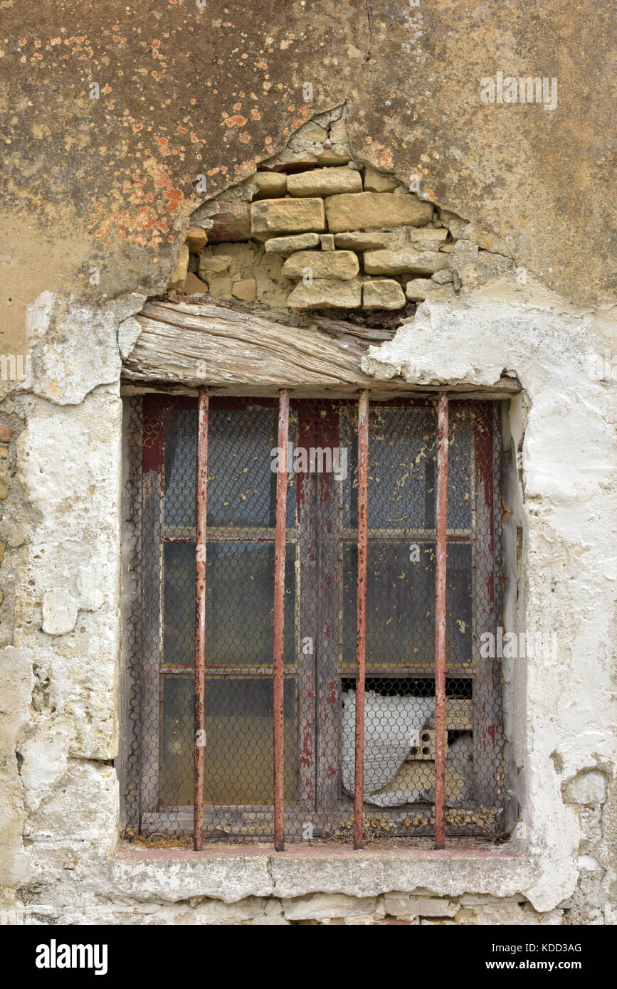a barred window with cracked plaster and broken glass showing neglect ...