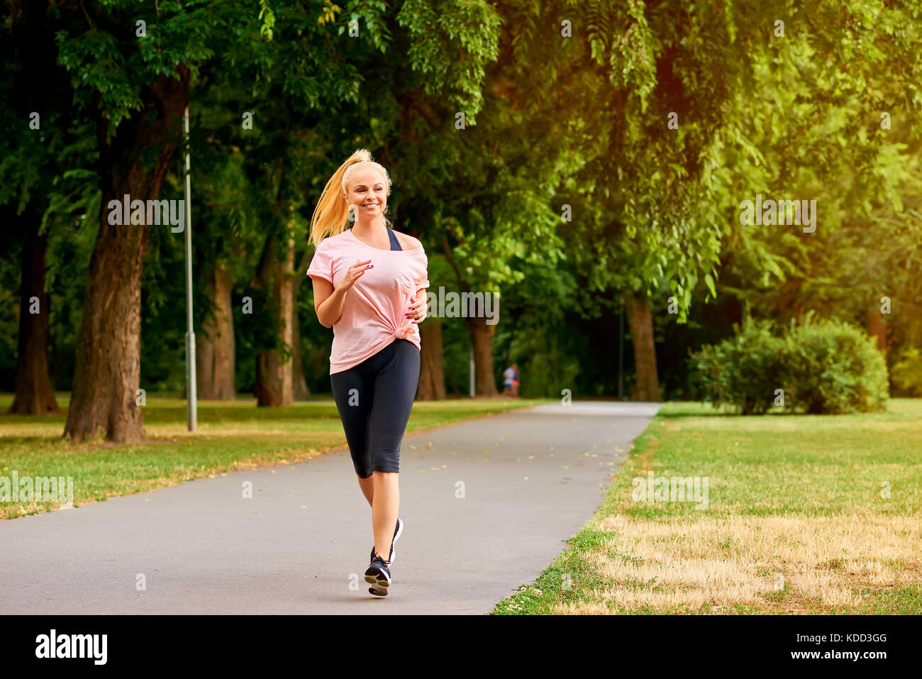 A beautiful young blonde woman running on the road in a park Stock ...