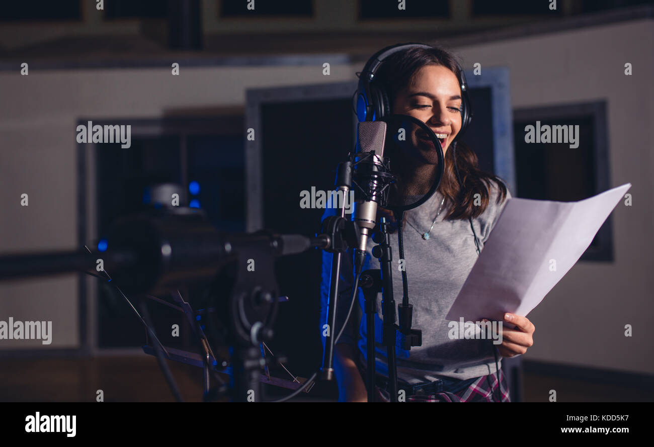Smiling female singer with microphone and reading lyrics. Woman ...