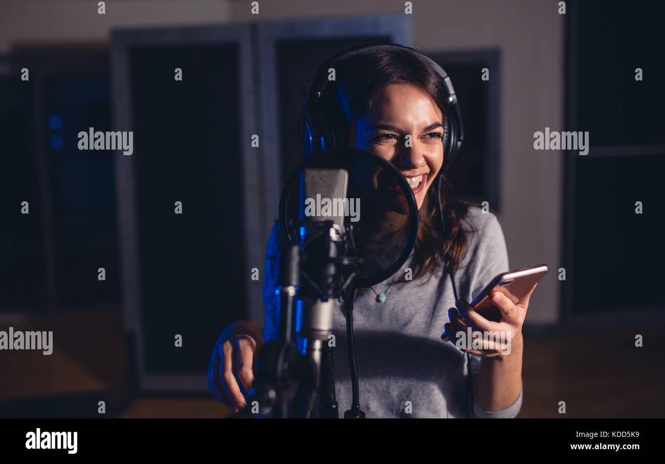 Smiling female playback singer with microphone and mobile phone in ...