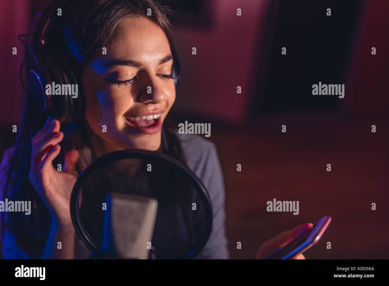 Female singing a sing with mobile phone at recording studio. Young ...