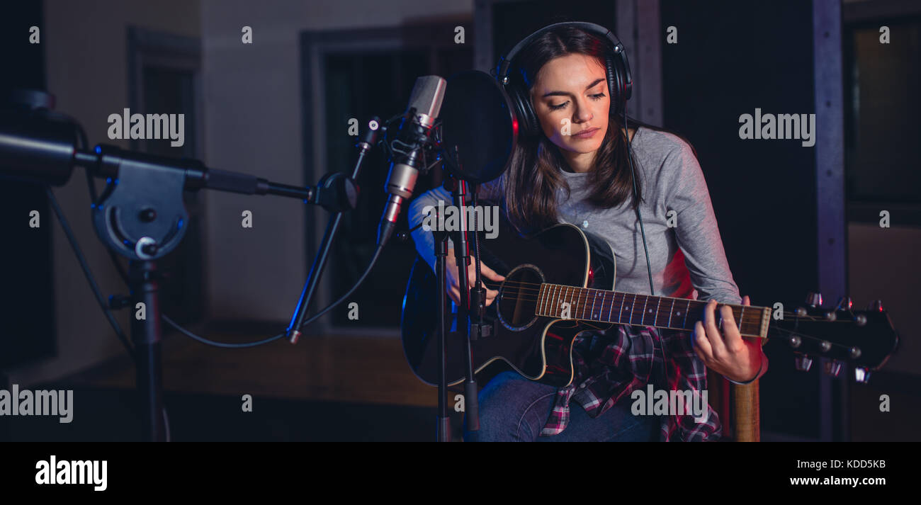 Female singer performing a song in studio and playing guitar. Woman ...