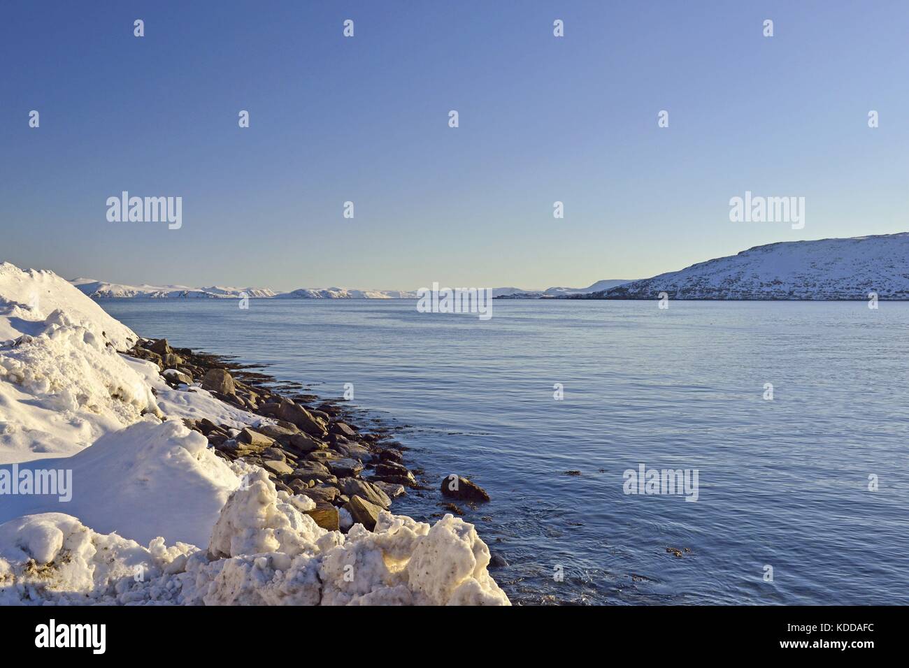 Snow-covered waterside by the strait Havøysund and the deep blue water ...